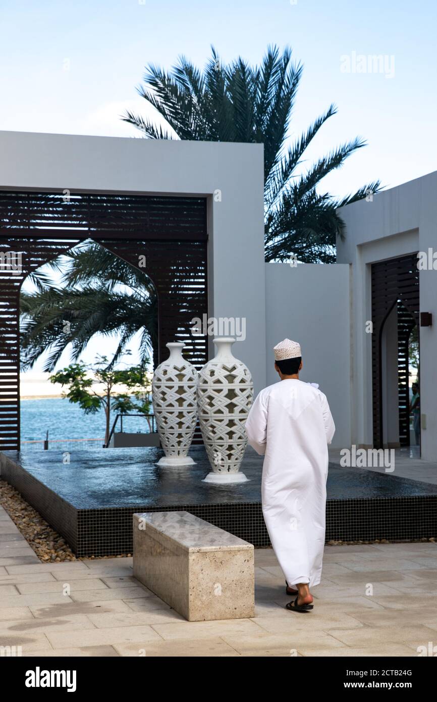 An Omani man in his dishdasha walking by water features towards the ...
