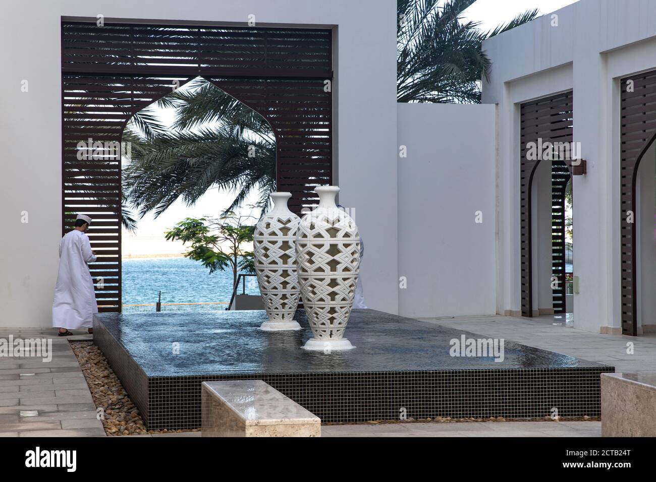 An Omani man in his dishdasha walking by the marina. Fountain water ...