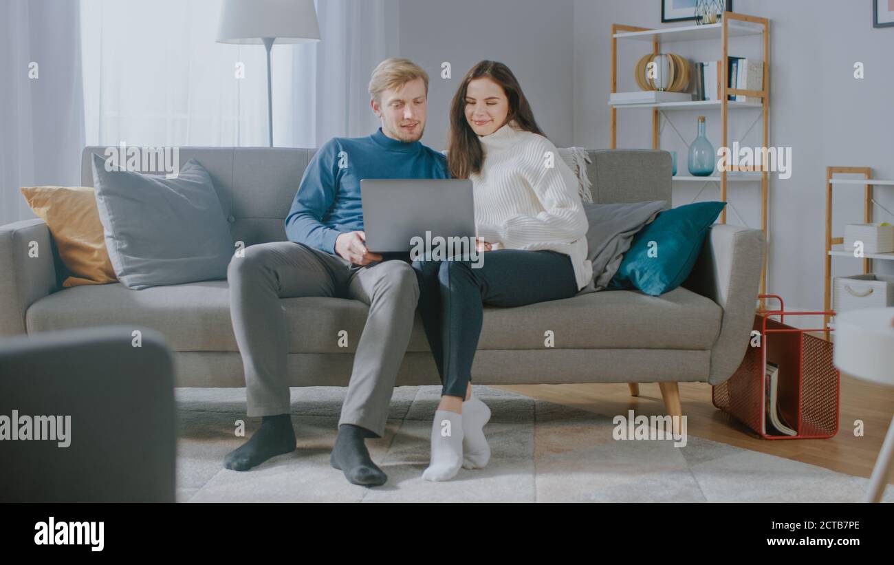 Cute Young Couple Use Laptop Computer, while Sitting on the Couch in ...