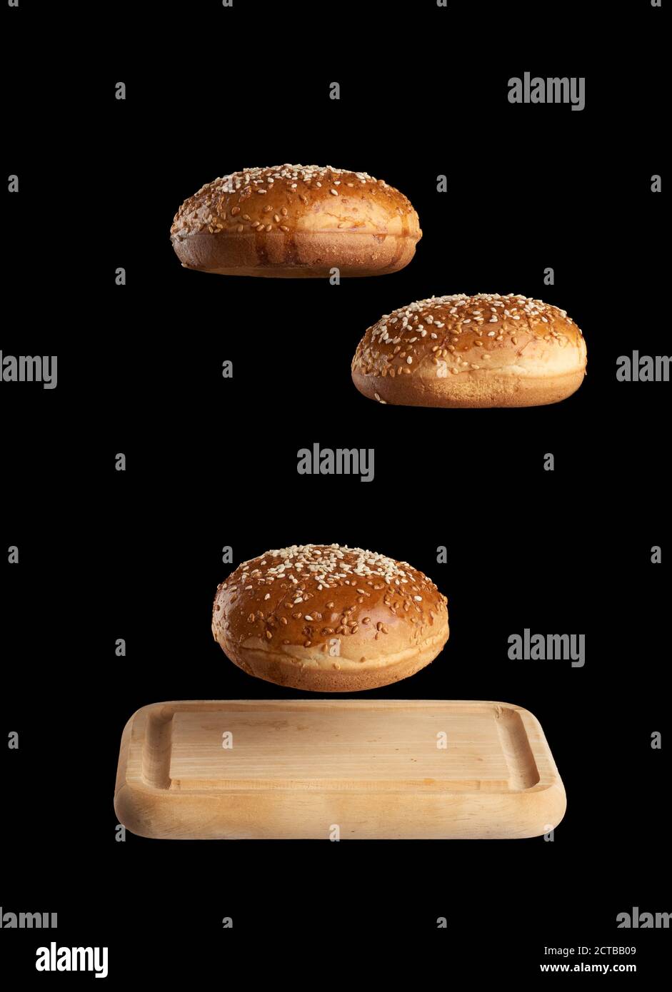 baked round bun with sesame seeds hover over brown wooden cutting board ...