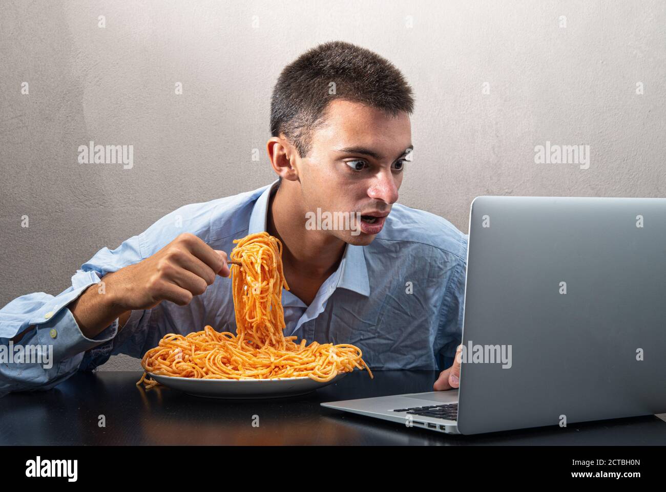a man eating spaghetti with tomato sauce and watching the computer ...