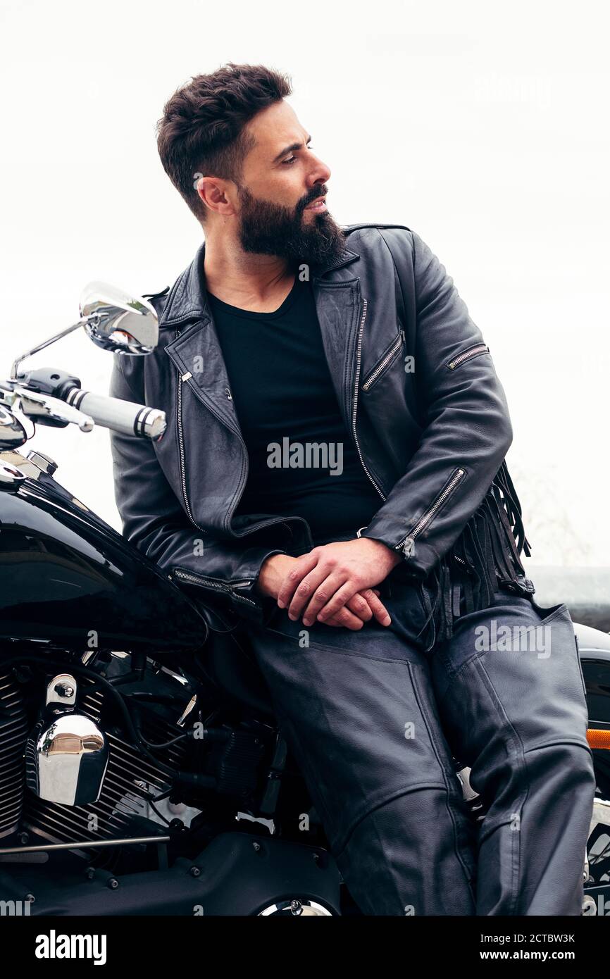 vertical photo of a handsome bearded man dressed in leather rests on ...