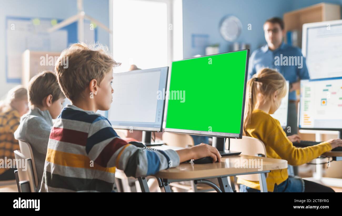 Elementary School Computer Science Classroom: Cute Little Boy Uses Green Mock-up Screen Computer ...
