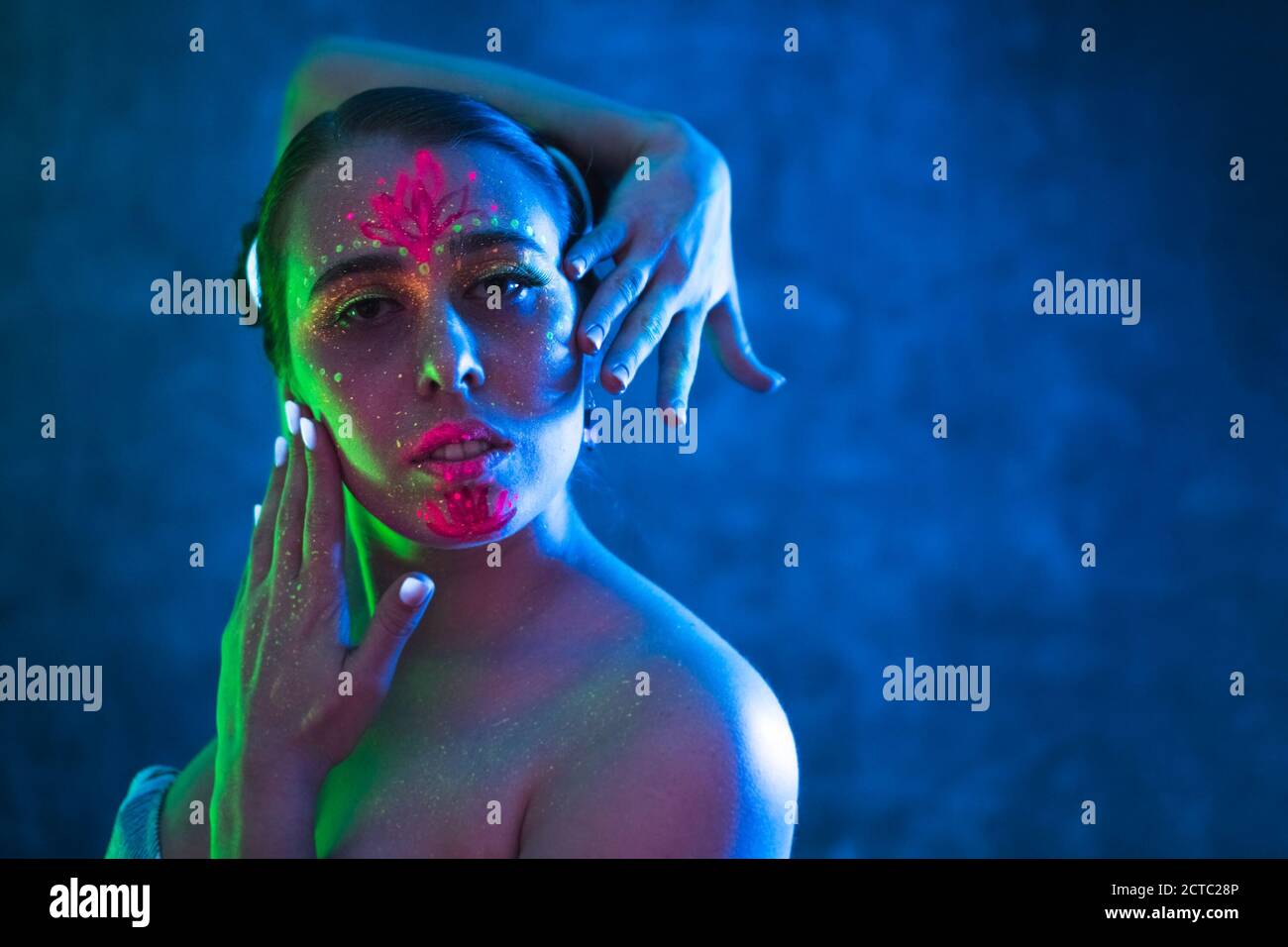 Portrait of beautiful young woman with fluorescent makeup on face and ...