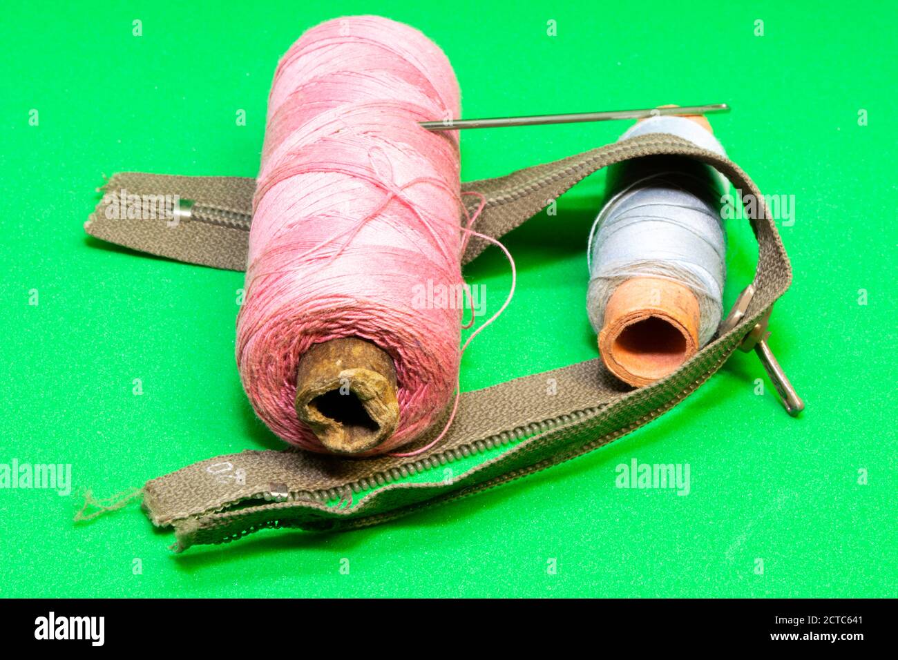 two spools of colored threads, a needle and a zipper on a green ...