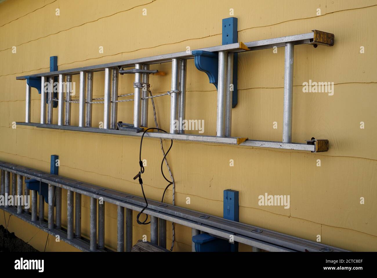 The ladders are hung up on the yellow exterior wall Stock Photo - Alamy