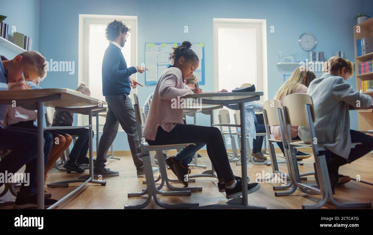 In Elementary School Class: Enthusiastic Teacher walks between Rows of ...