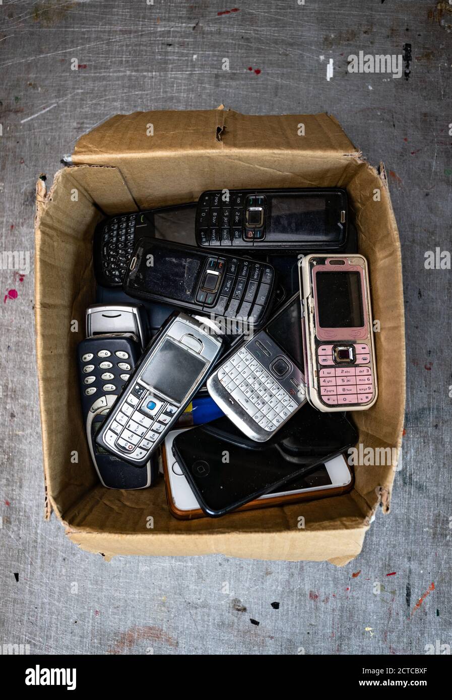 old, obsolete and broken cellphones in a cardboard box. scratched metal ...