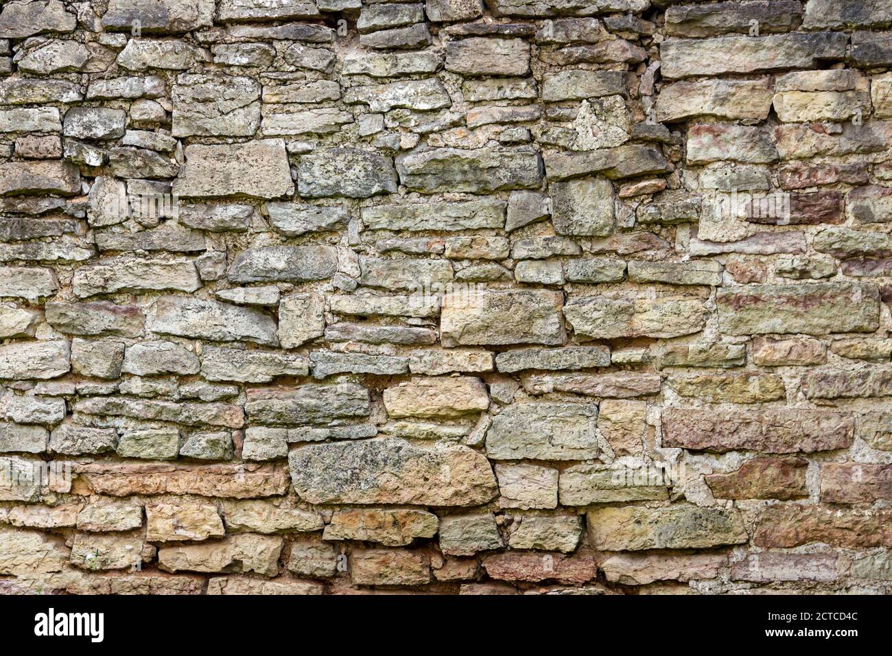 The surface of an old stone wall, masonry of uneven wild hewn stones ...