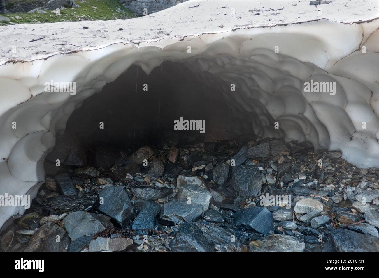 Melt hole under snow patch in apine region, water dripping on rocks ...