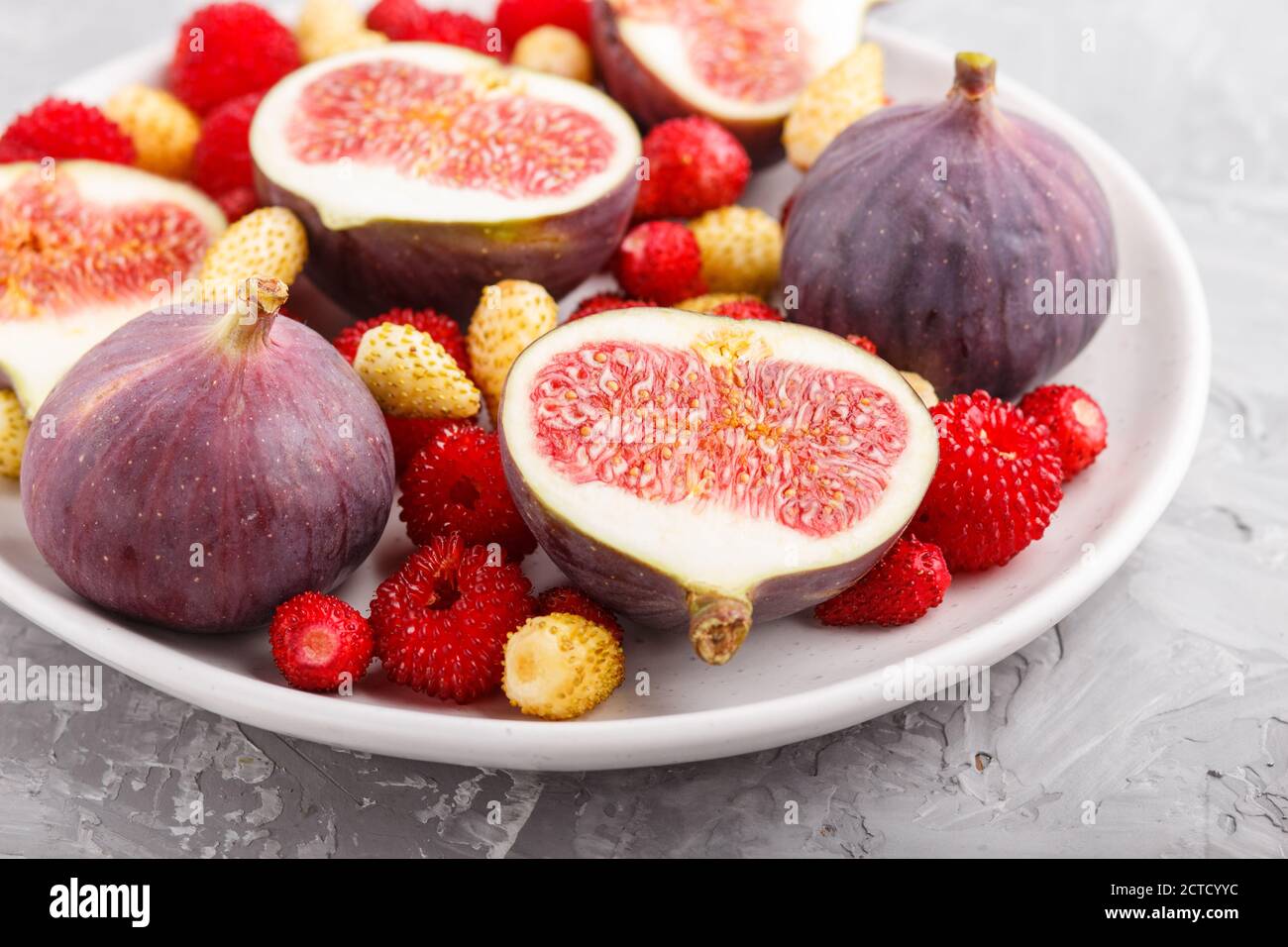 Fresh figs, strawberries and raspberries on white ceramic plate on gray ...