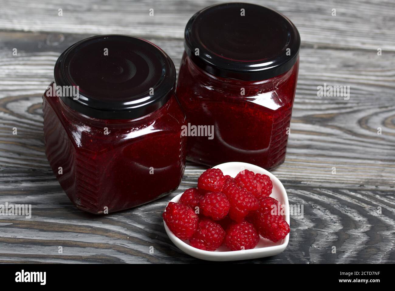 Raspberry jam in glass jars. Nearby are raspberries in a saucer. On ...
