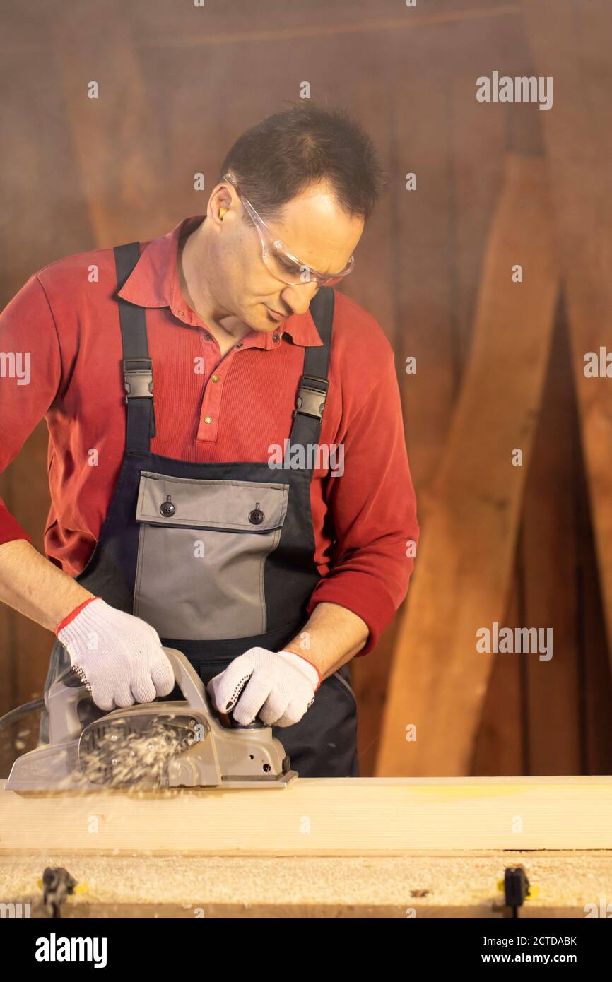 middle-aged male carpenter in googles working on workbench with ...