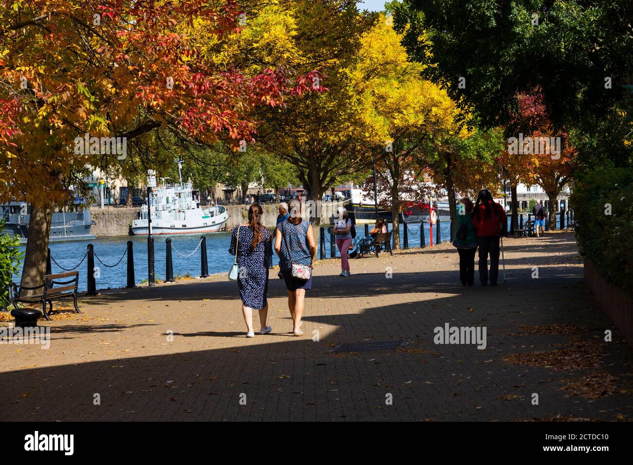 Pedestrians walk in the autumn sunshine with leaves changing colour ...