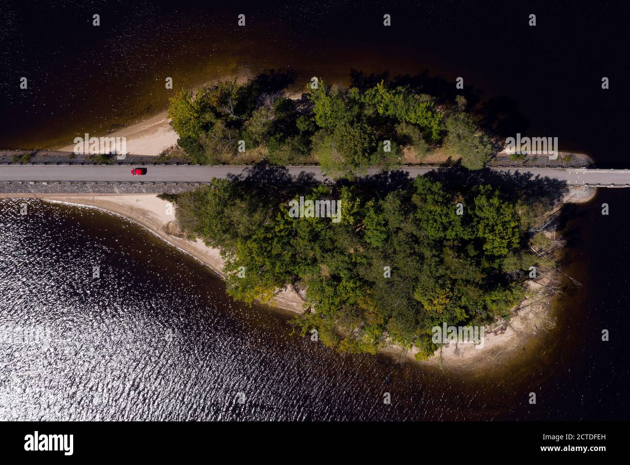 Aerial photo of a red car driving on a road that crosses a remote tiny ...