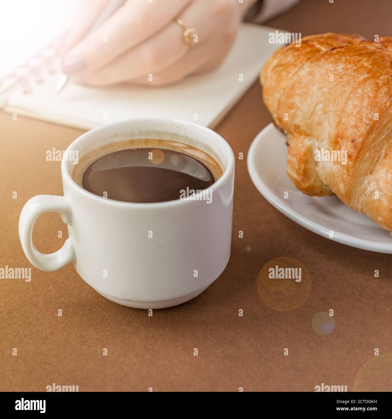 Close up of croissant and espresso. Woman writing on notebook ...