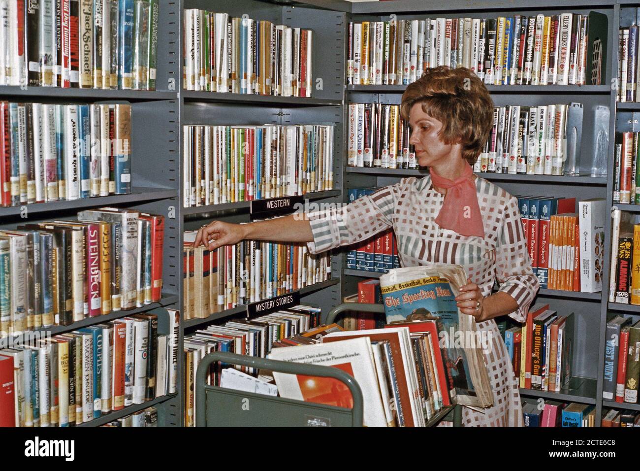 A librarian is pulling books from a library book shelf ca. 1976 Stock ...