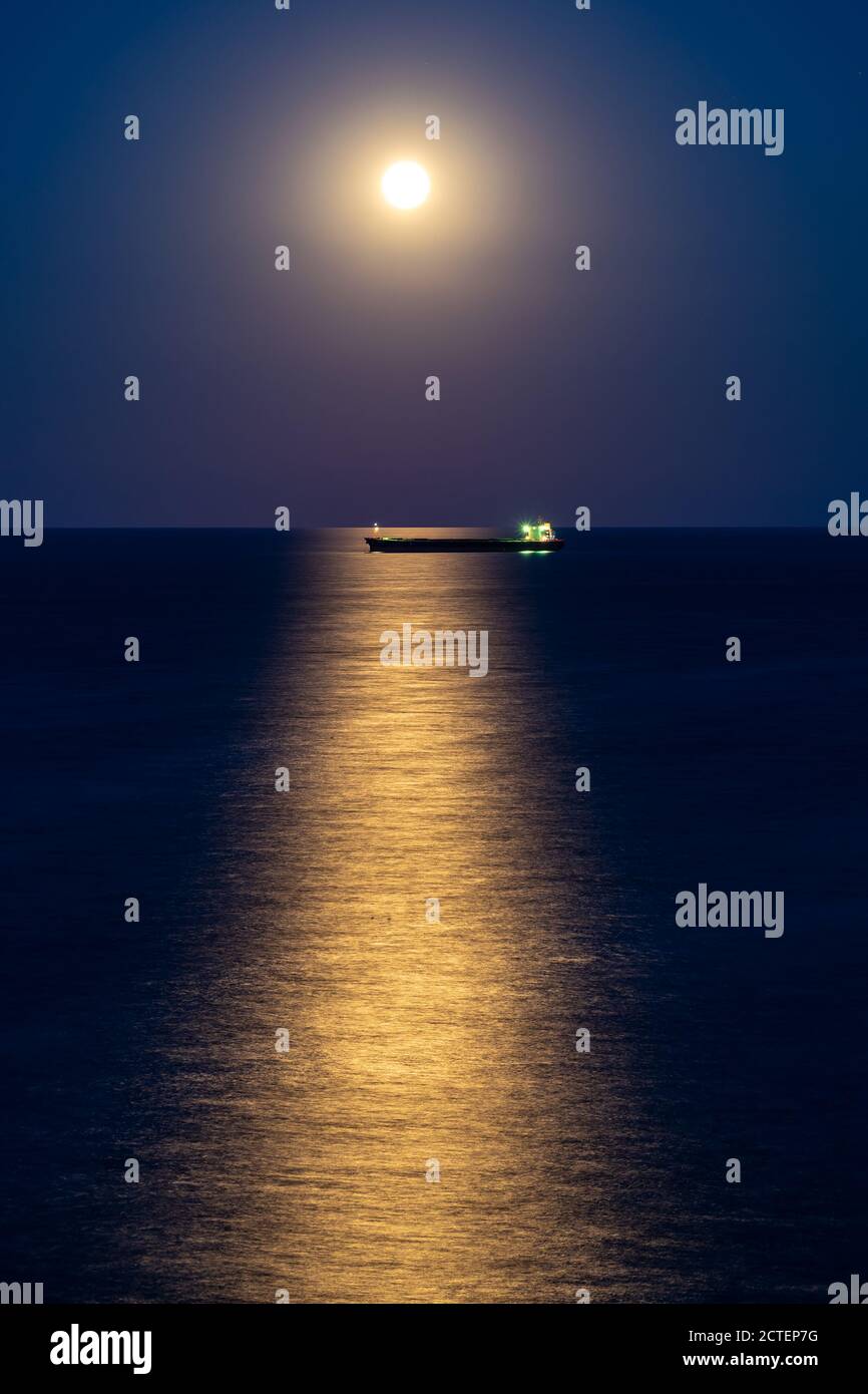 Cargo ship at night with full moon over the horizon Stock Photo - Alamy
