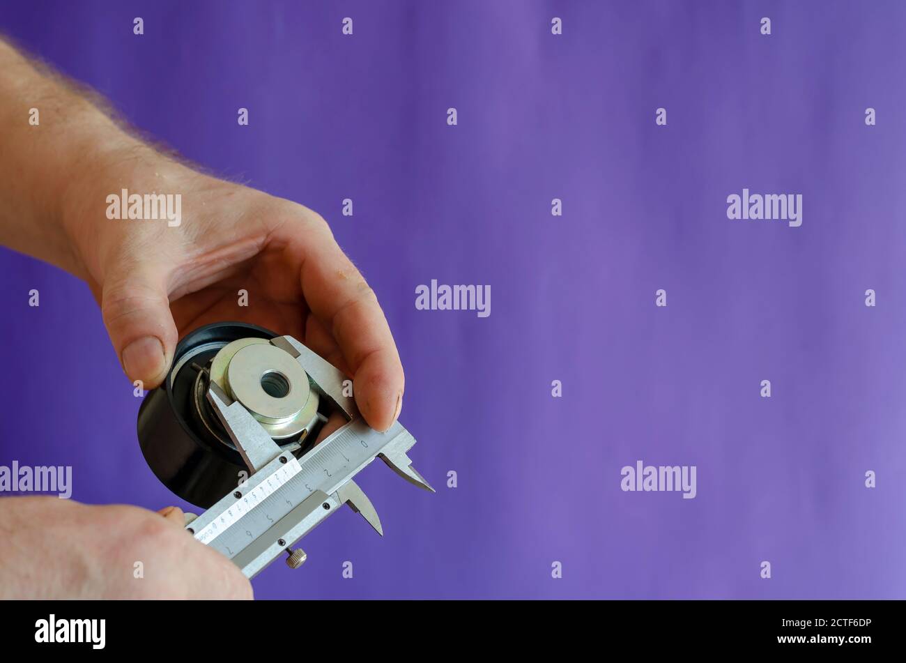 Vernier caliper and timing belt tensioner in hand on blue background ...