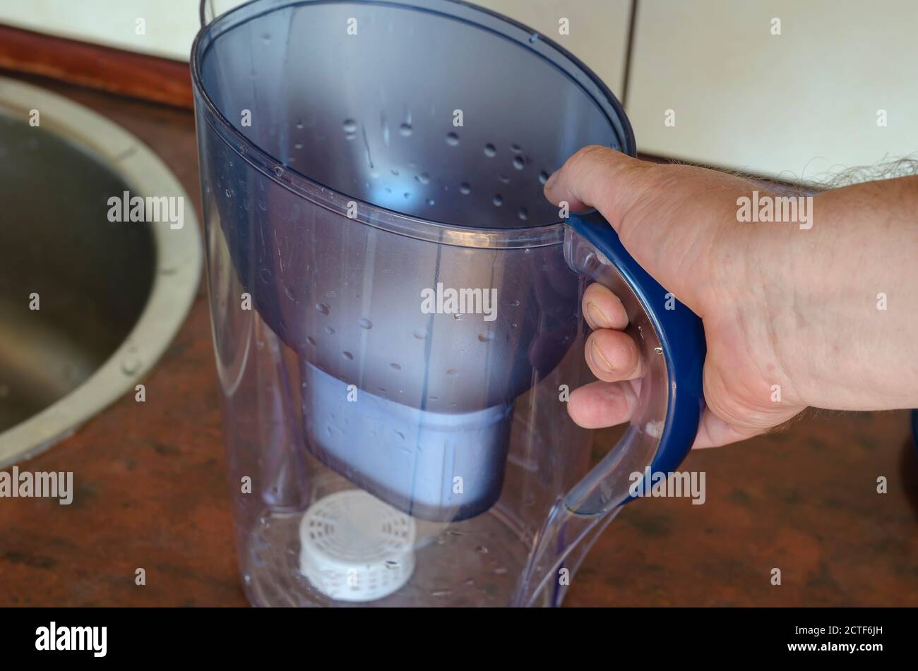 An empty water jug in hand next to the sink. A plastic water jug ready ...