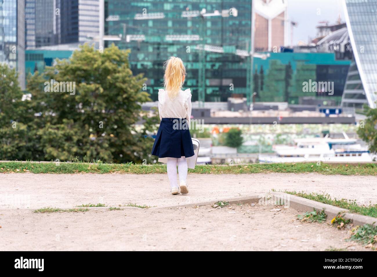 a little girl in business clothes whish schoolbag stands alone against ...
