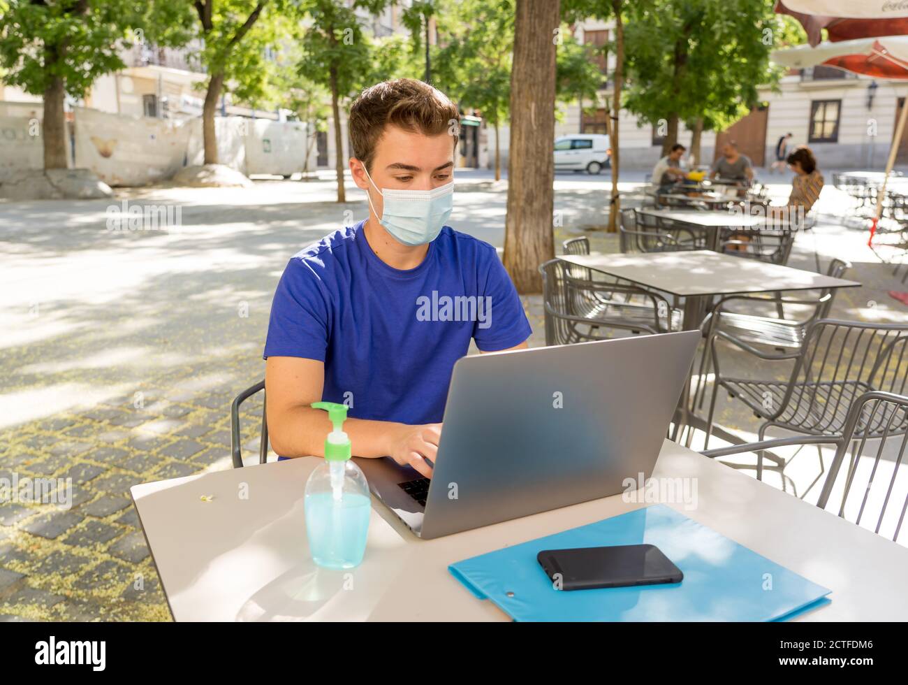 Young man wearing protective face mask and using hand sanitizer while ...