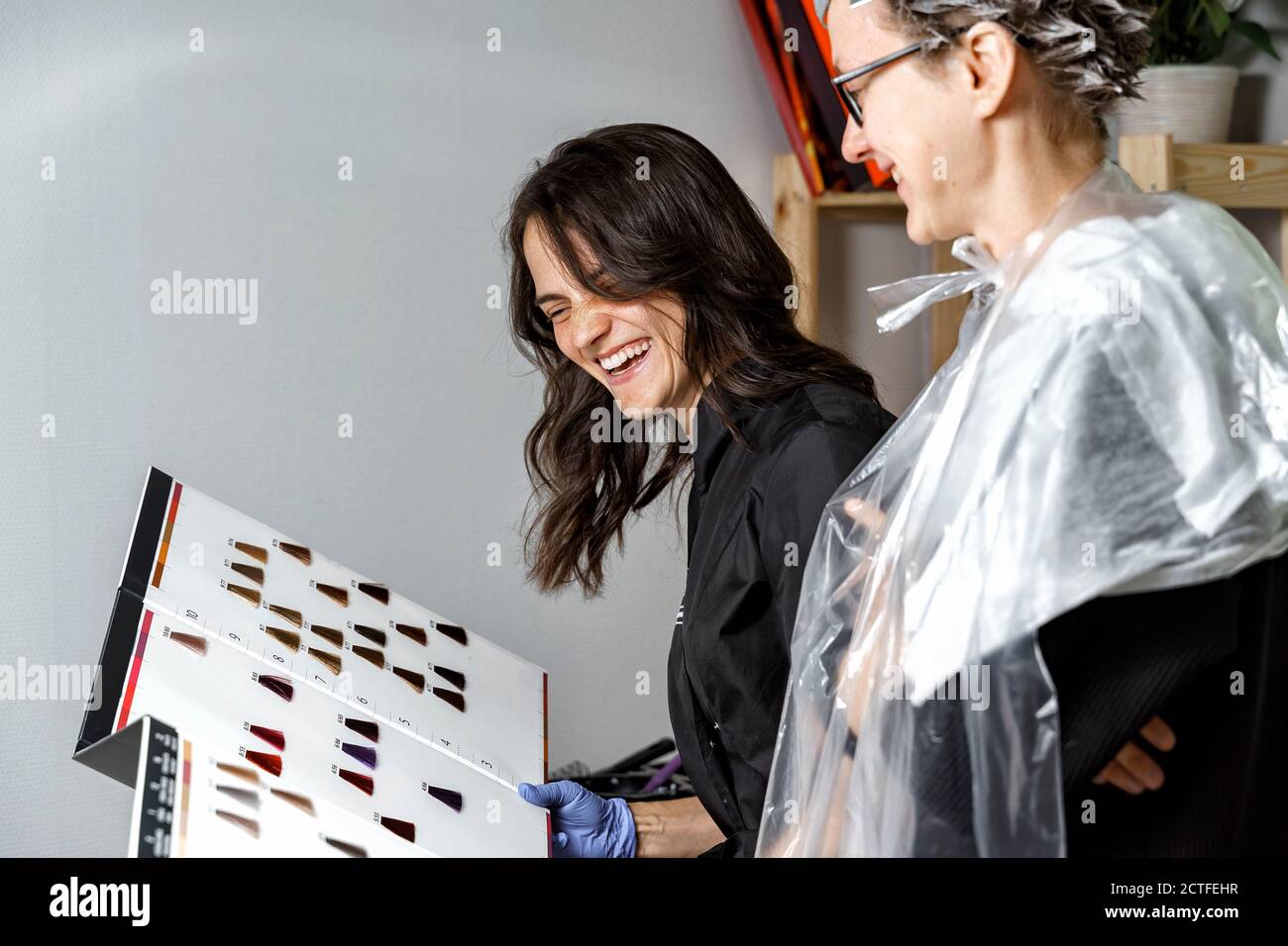 cute beautiful hairdresser laughs and helps young woman choose a shade ...