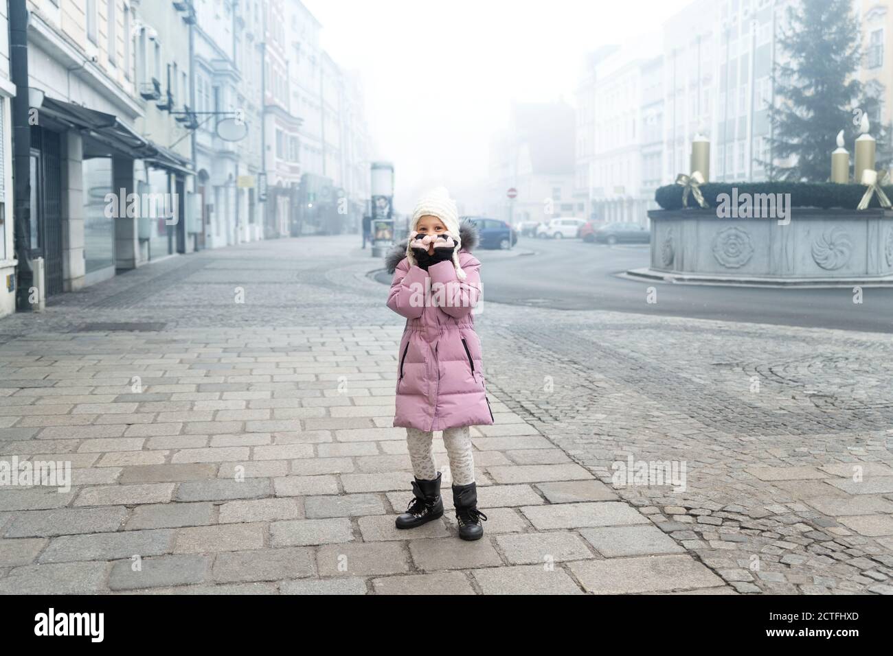 Cute liitle sad lost caucasian girl in warm long pink jacket and hat ...
