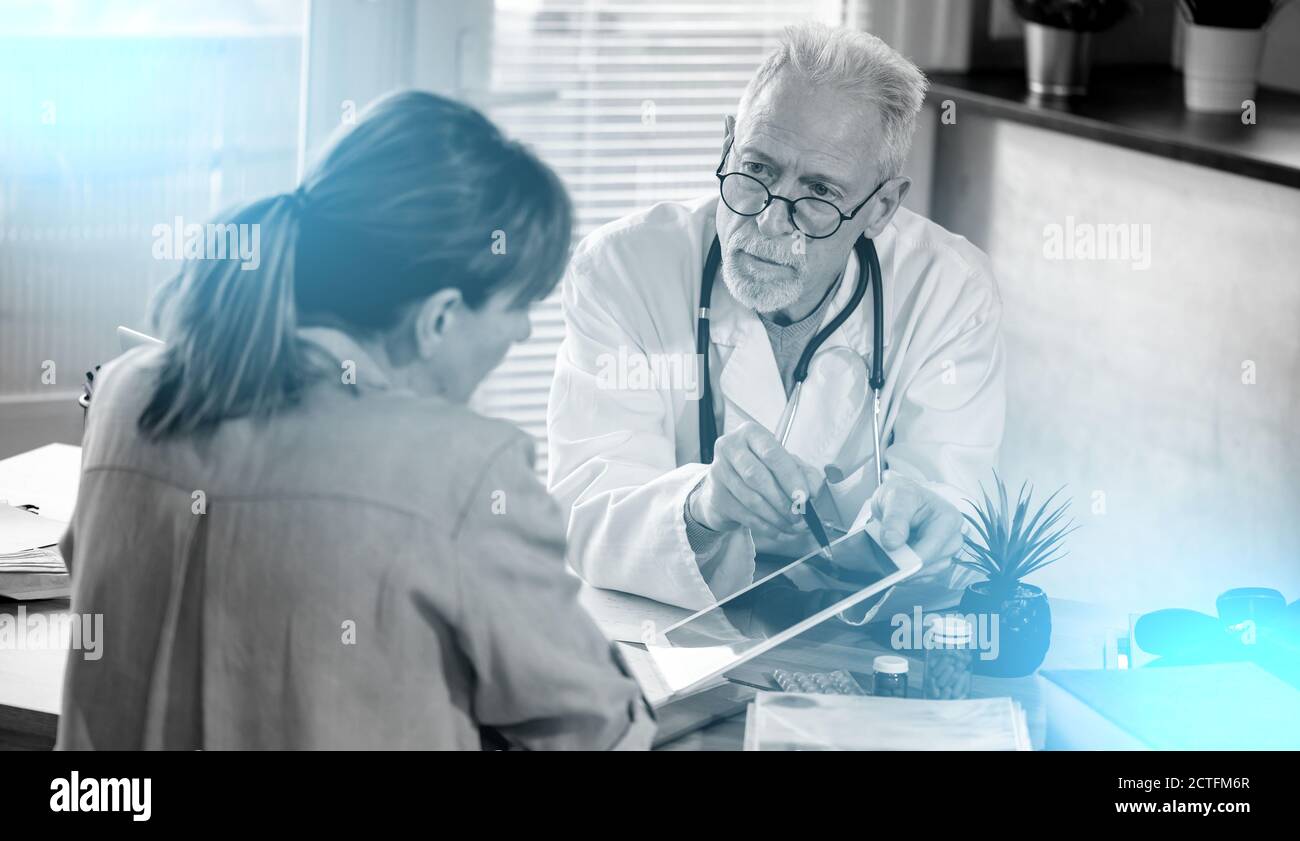 Senior doctor showing reports on digital tablet to his female patient ...