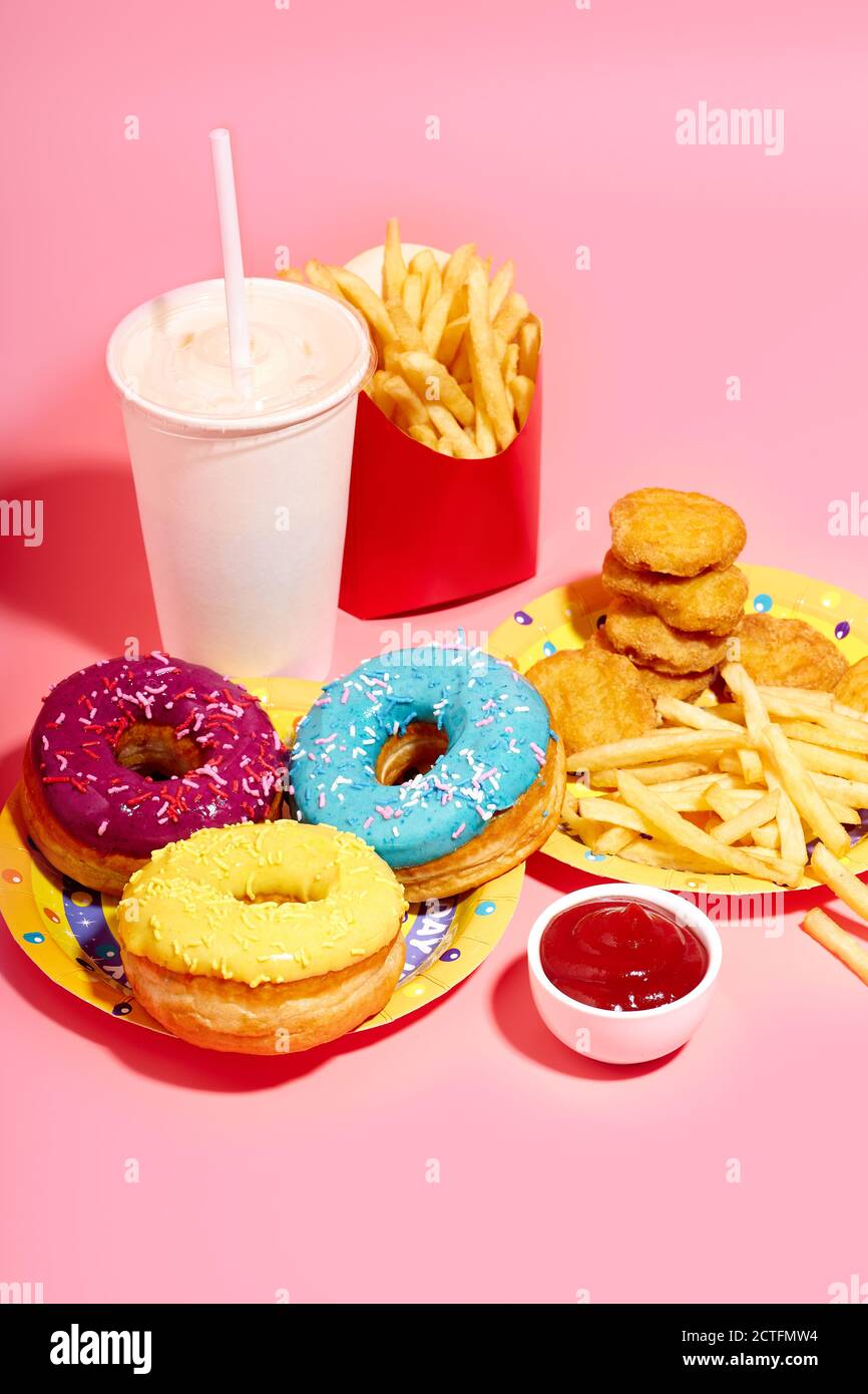 Junk food meal on pink background. French fries, chicken nuggets, sweet ...