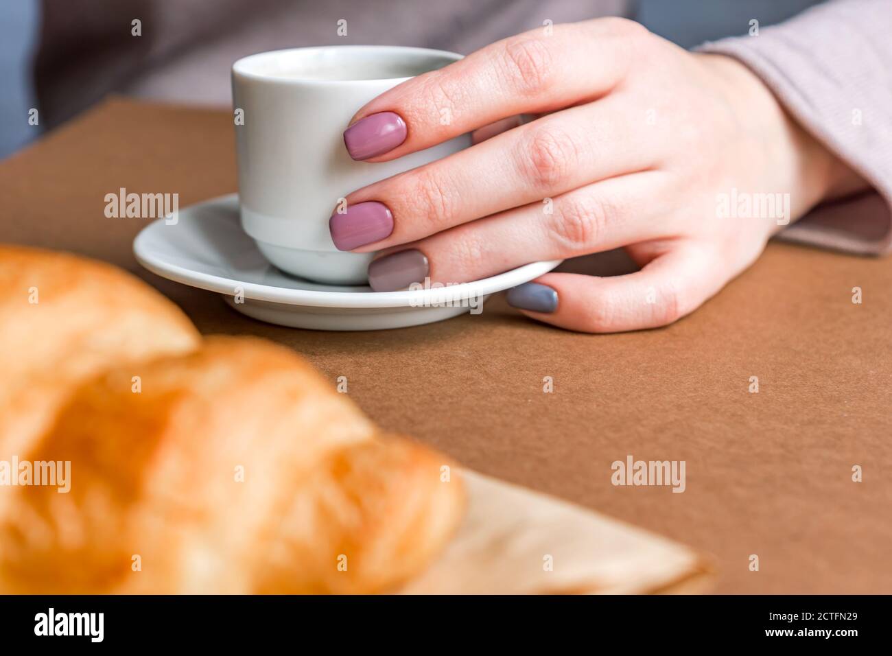 Female hands with manicure holding cup of coffee and eating croissant ...