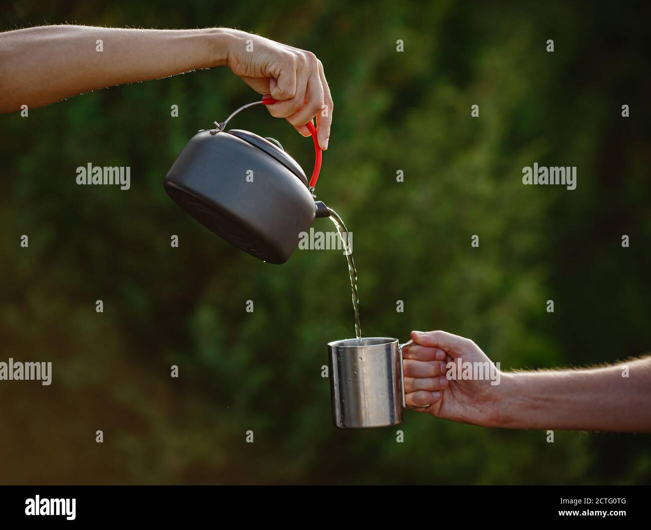 Hiker pouring a hot drink from a metal teapot into a steel mug ...