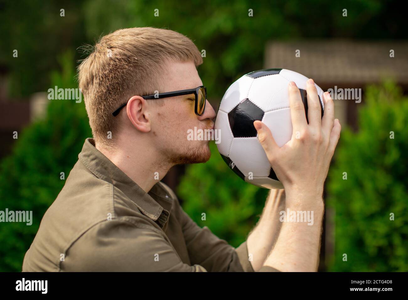 Football fan celebrates success kissing soccer ball on green backdrop ...