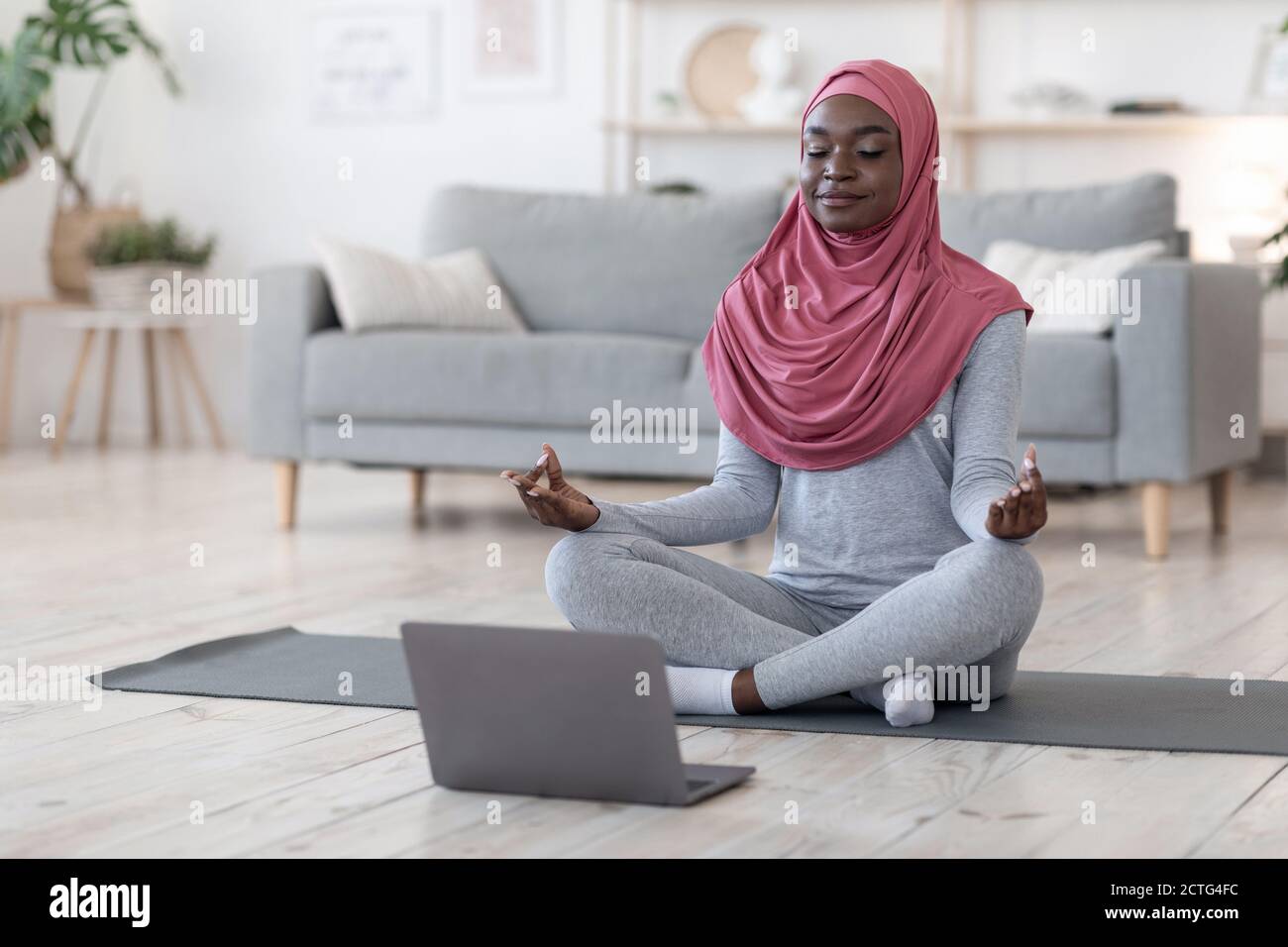 Yoga online. Black muslim woman meditating in front of laptop at home ...