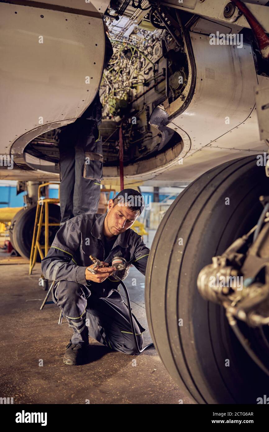 Confident Caucasian mechanic working at an airplane hangar and fixing ...