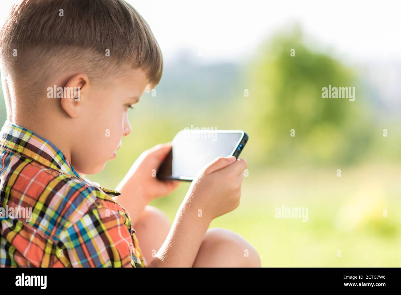 The child looks into the phone while sitting in the summer on the ...