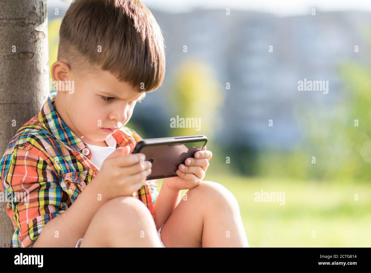 The child looks into the phone while sitting in the summer on the ...