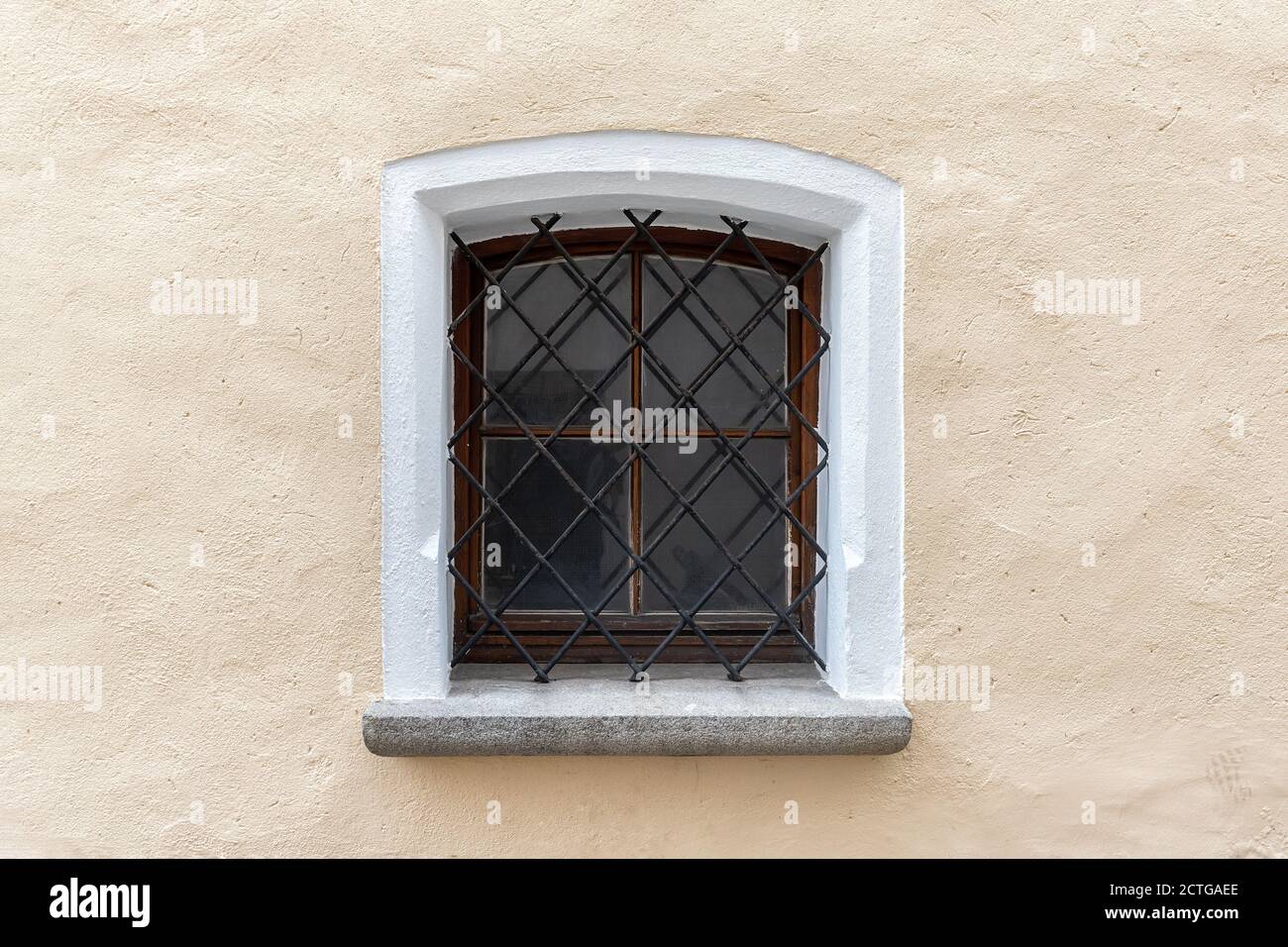 Old biege building wall with one small vintage window shuttered by iron ...