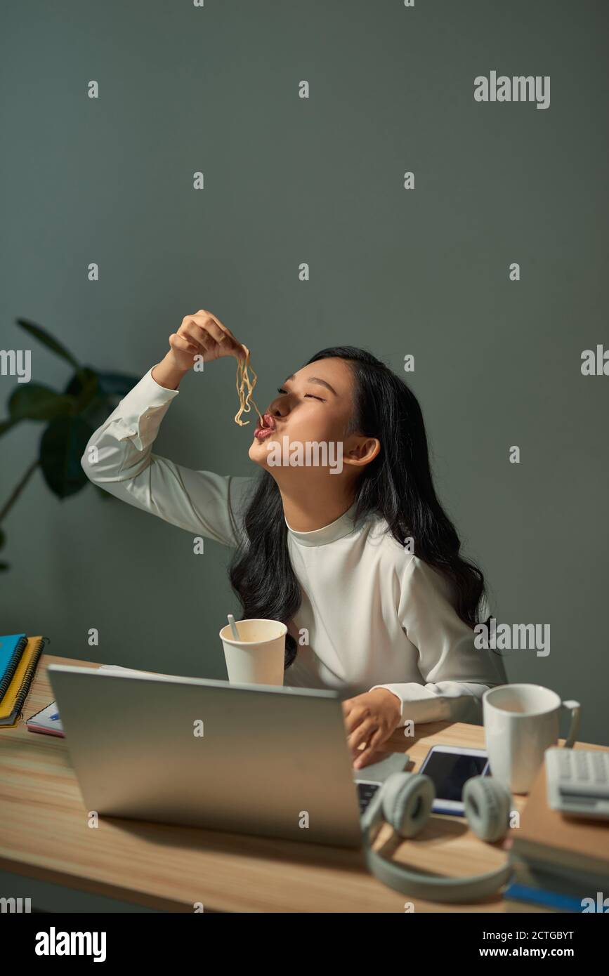 Hungry student eating noodle while learning at home Stock Photo - Alamy
