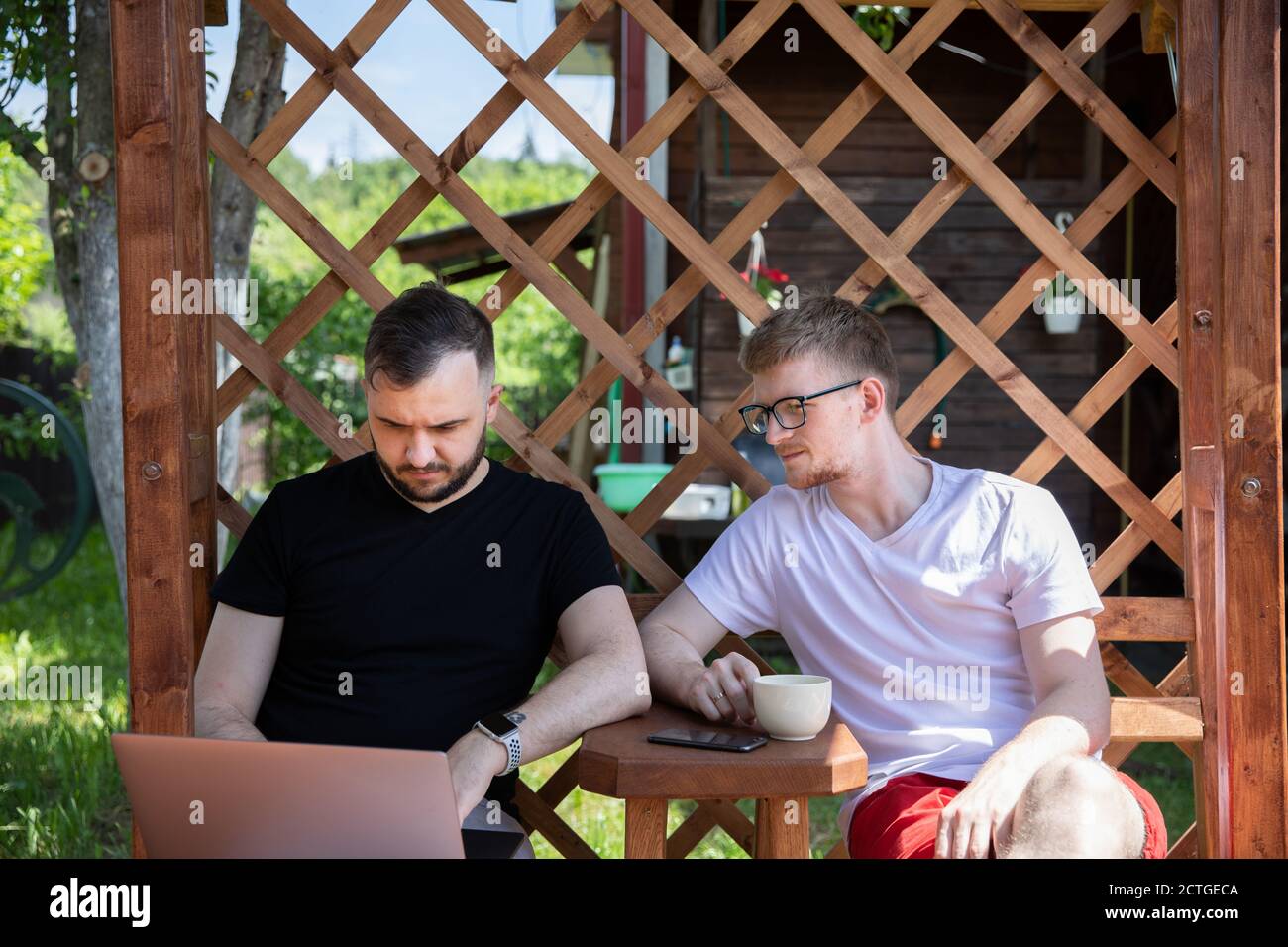 Young men work remotely outdoors in coutryside, two male collegues ...