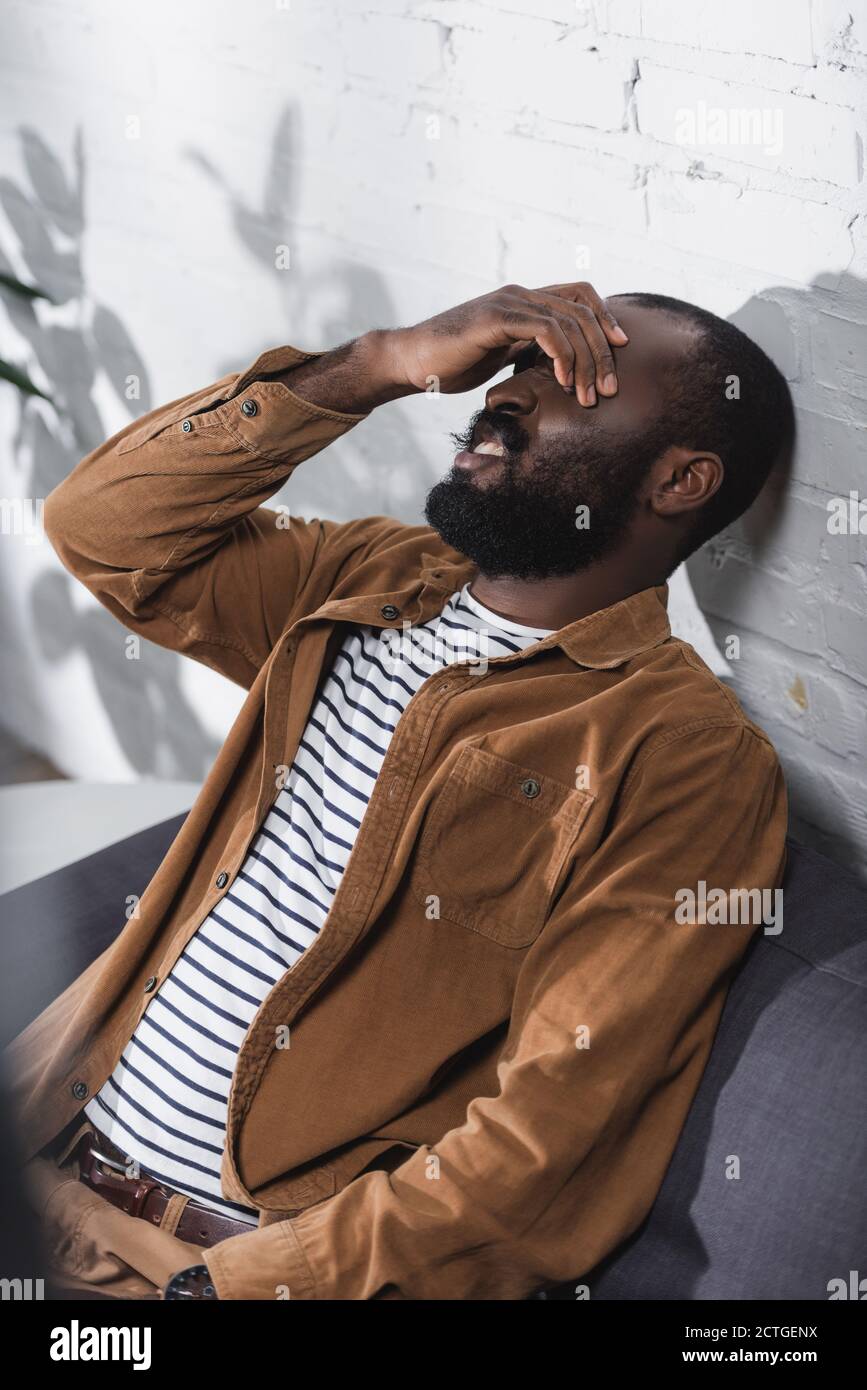 Selective focus of african american man touching eyes and sitting on ...