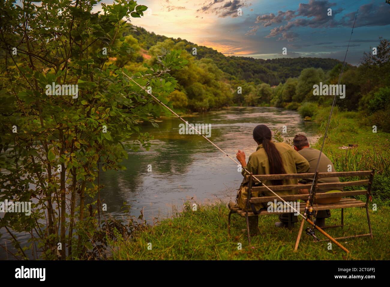 Friends sitting on a bench at a lake and fishing Stock Photo - Alamy