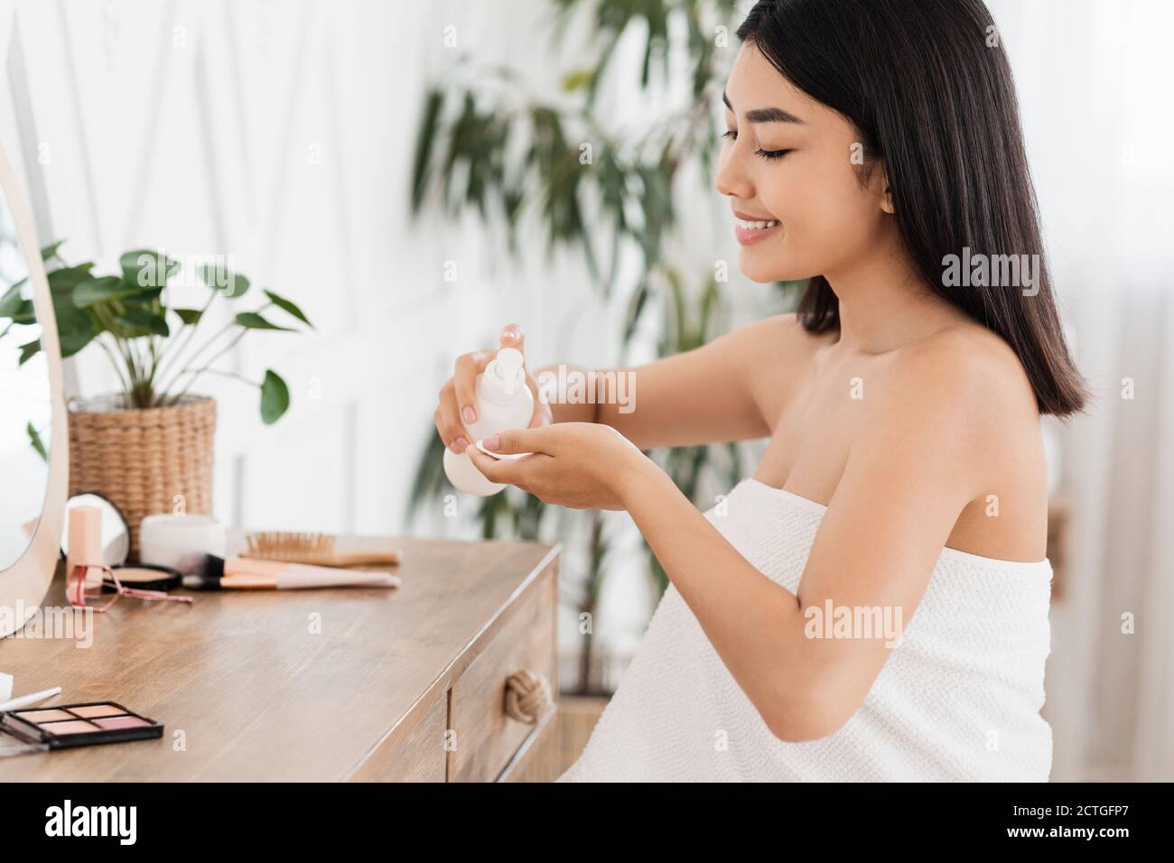 Cheerful asian woman cleaning her face with toner Stock Photo - Alamy