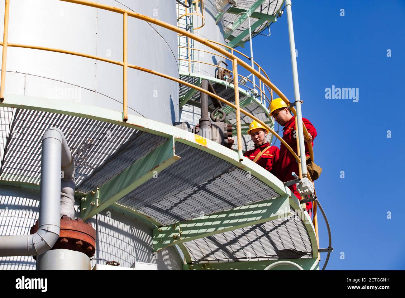 Two Asian maintenance workers in yellow hardhats and red work wear ...