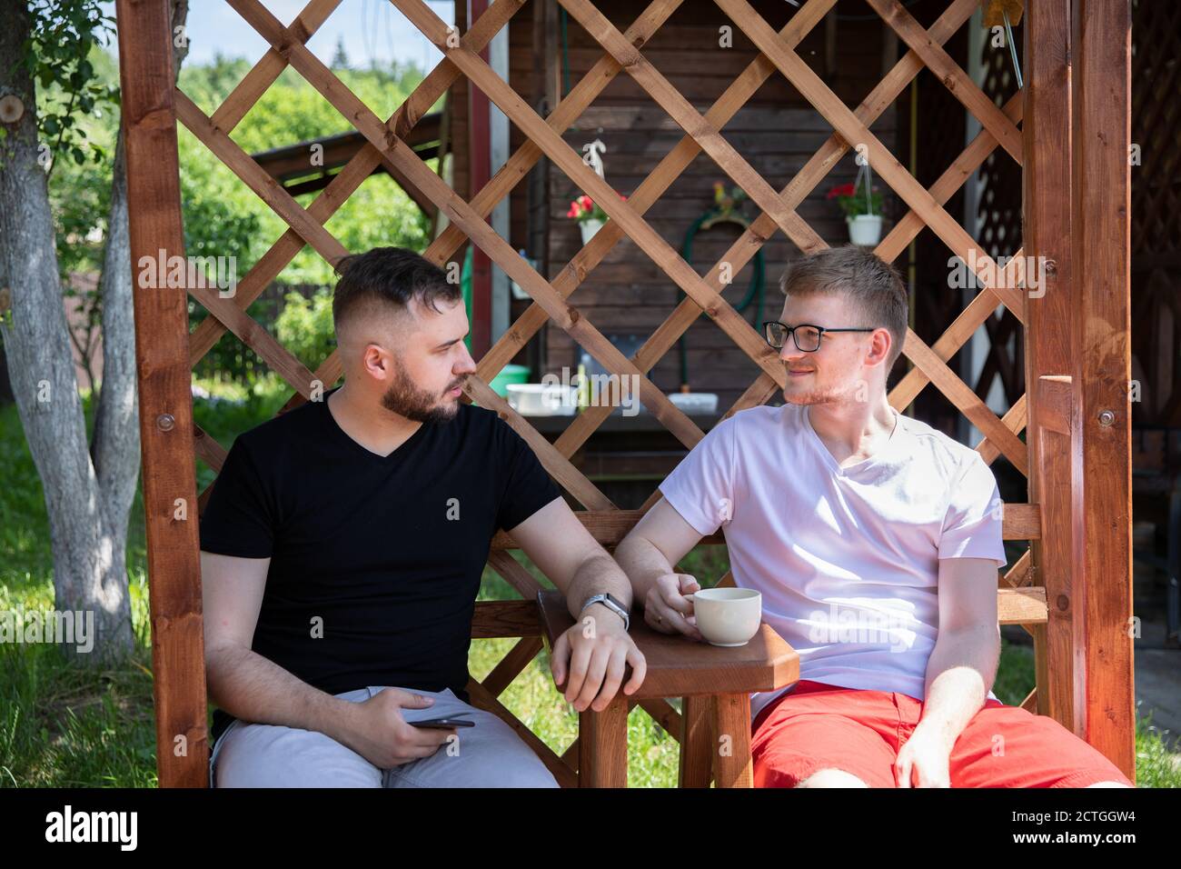 Two handsome guys sit on back yard of coutry house, male friends rest ...