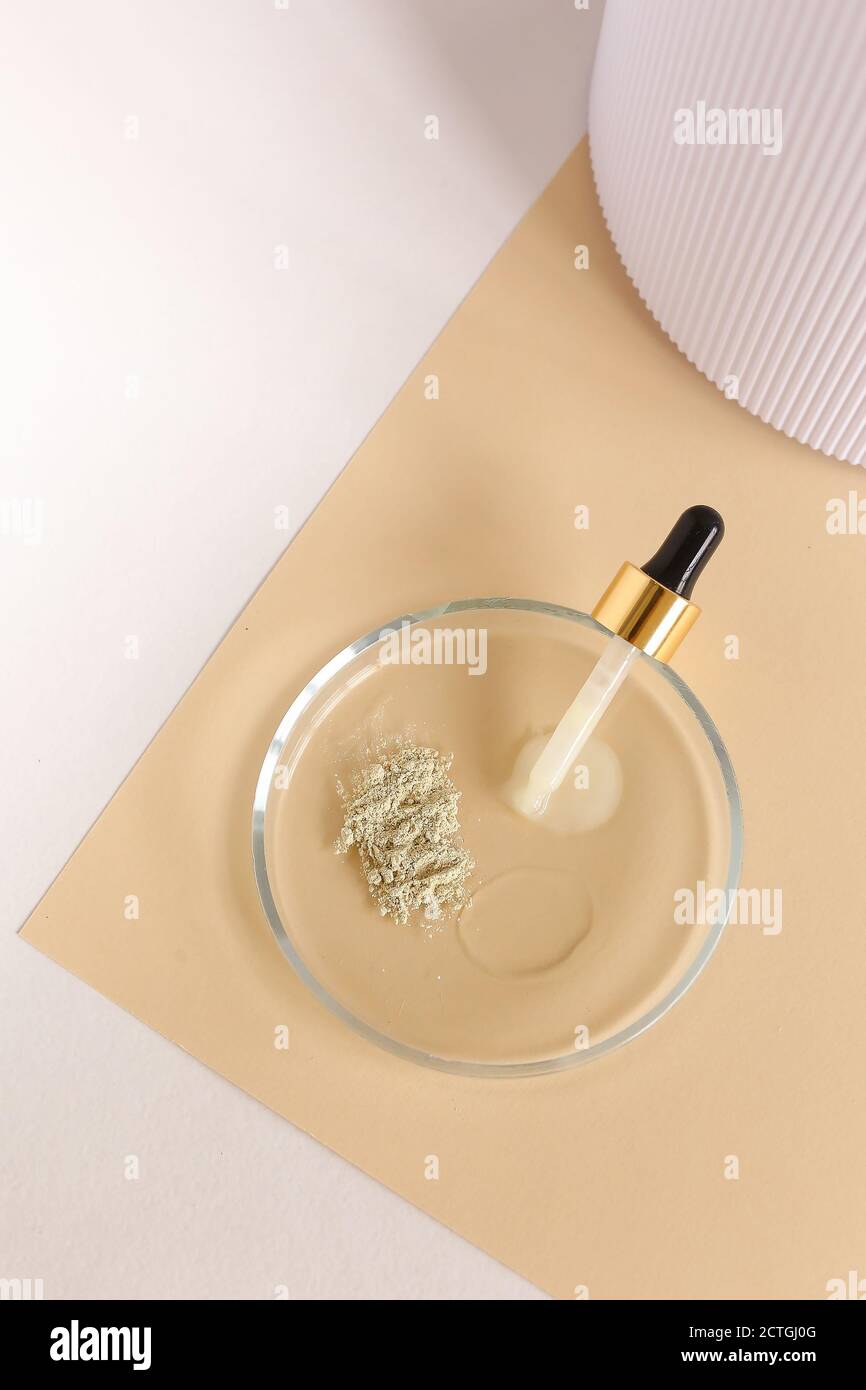 Clay powder and water in glass jar near pipette on beige and white ...
