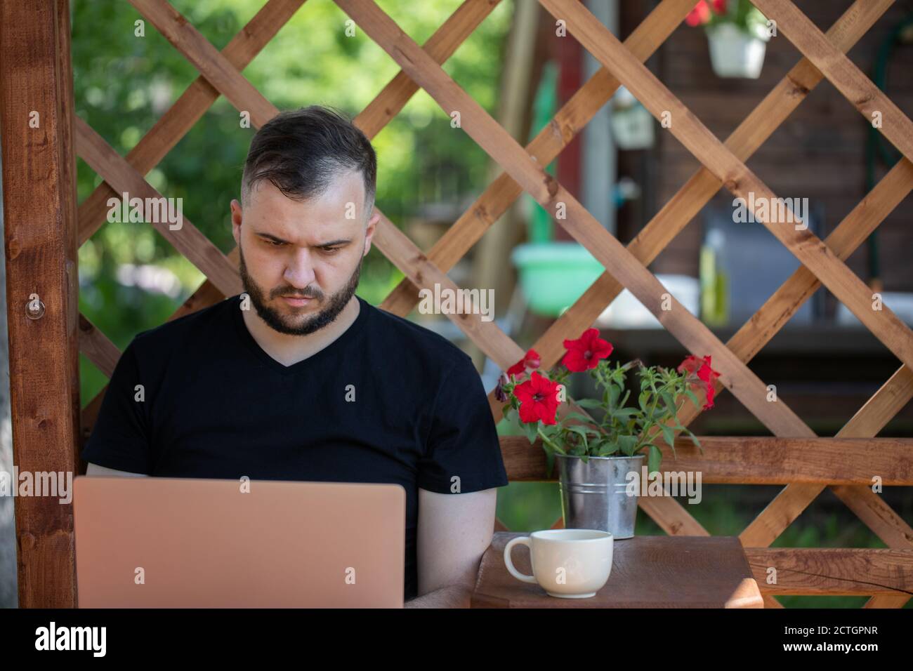 distance working concept young man works with laptop on wooden pergola ...