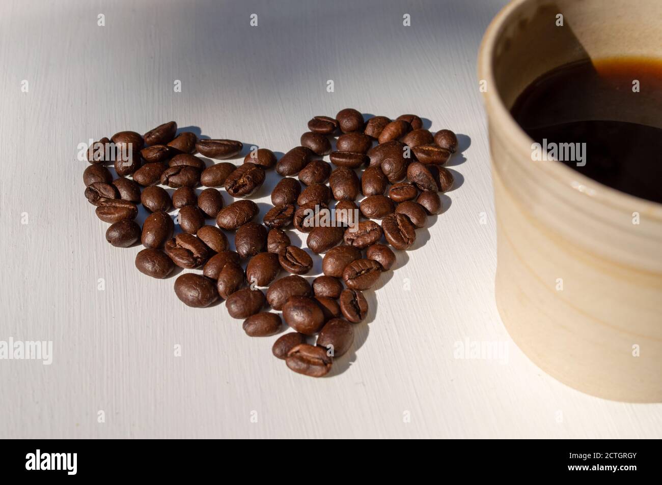 Close up of a heart formed by coffee beans next to a cub of coffee ...