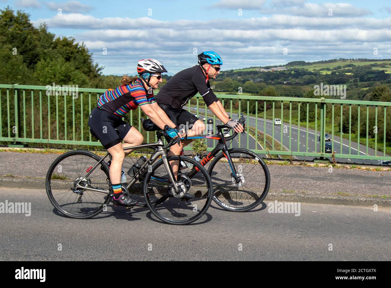 Man & woman cyclists riding Trek sports bike crossing above the M61 ...
