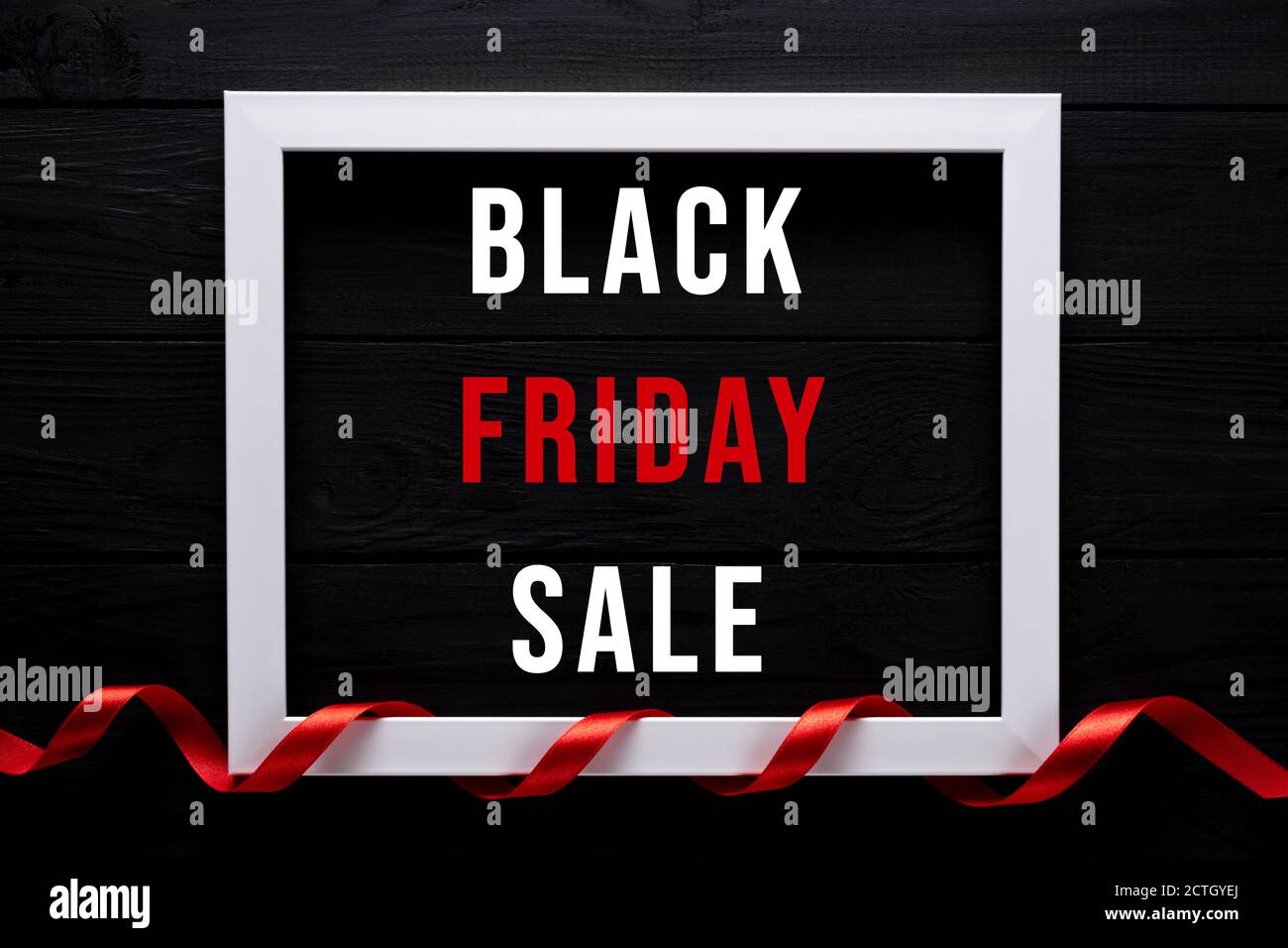 Black Friday. Top view of white photo frame with red ribbon on black ...